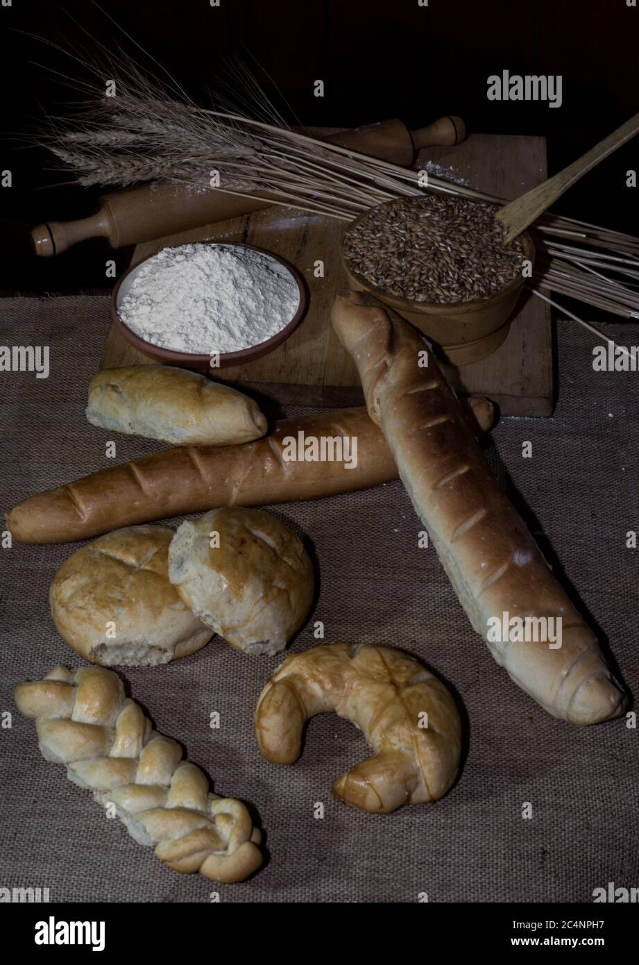 Different types of bread on the table with flour and wheat in bowls ...