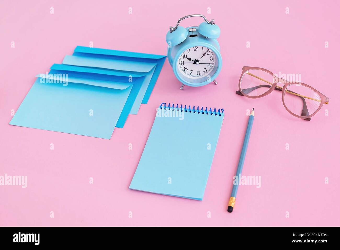 Blue correspondence envelopes, clock and notebook on pink background ...