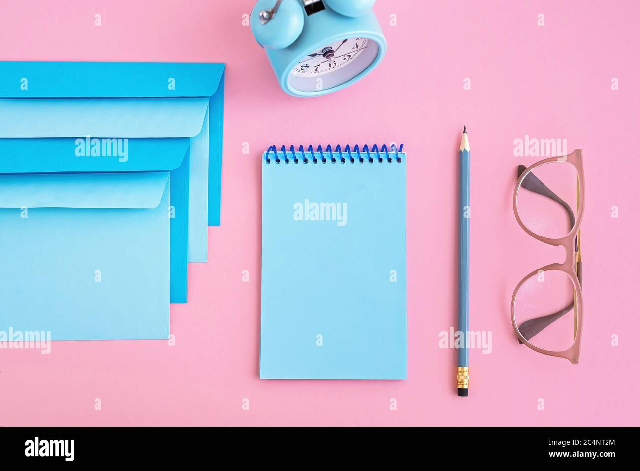 Blue correspondence envelopes, clock and notebook on pink background ...