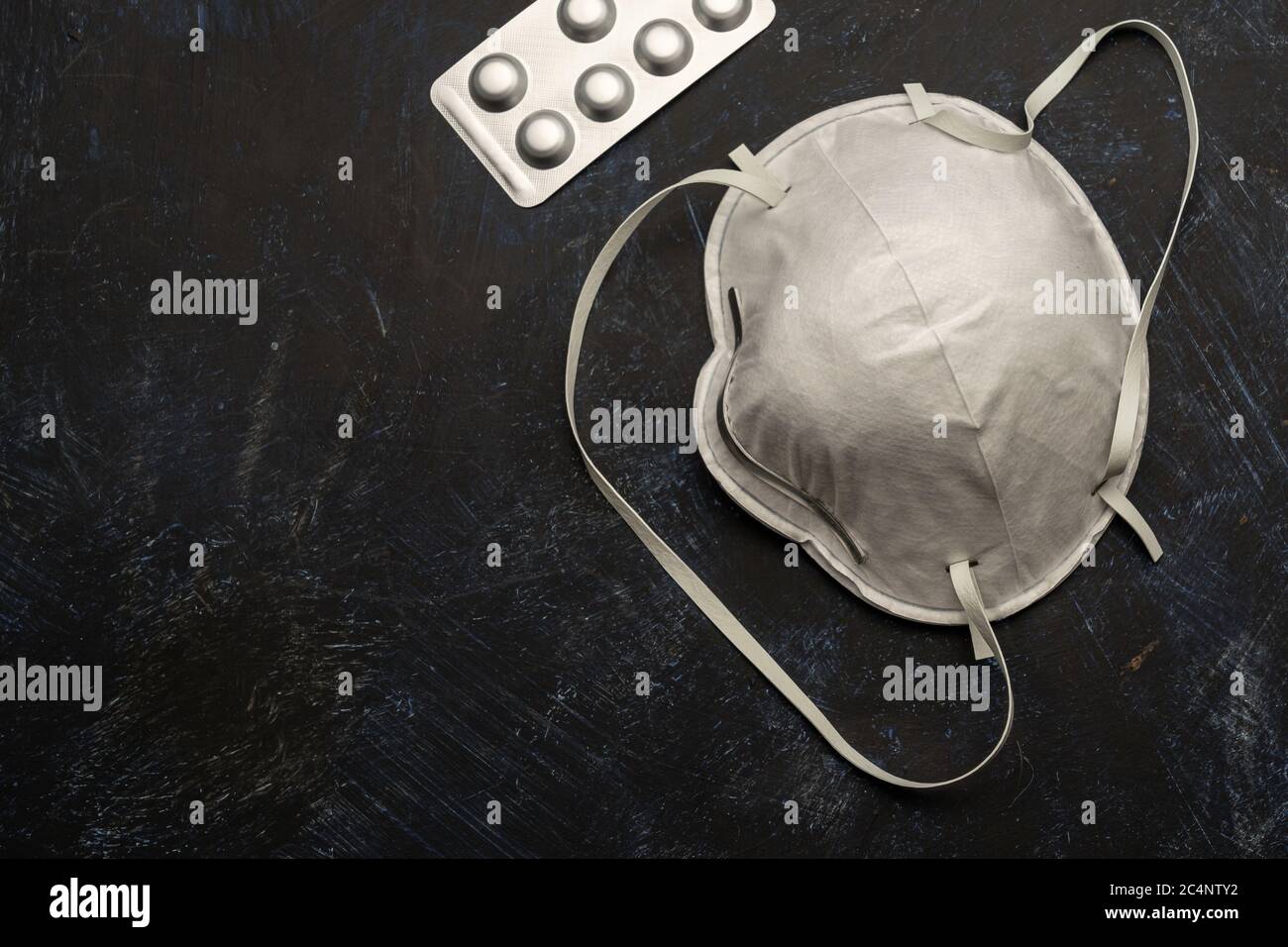 Grayscale closeup shot of a medical mask and pills on a black surface ...