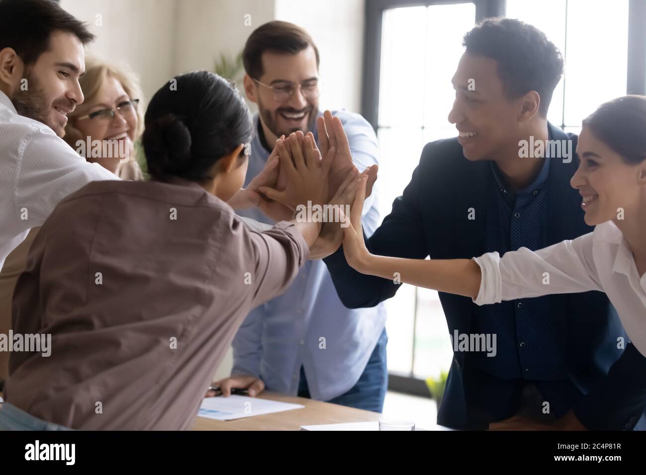Happy diverse employees joining hands, celebrating teamwork success at ...