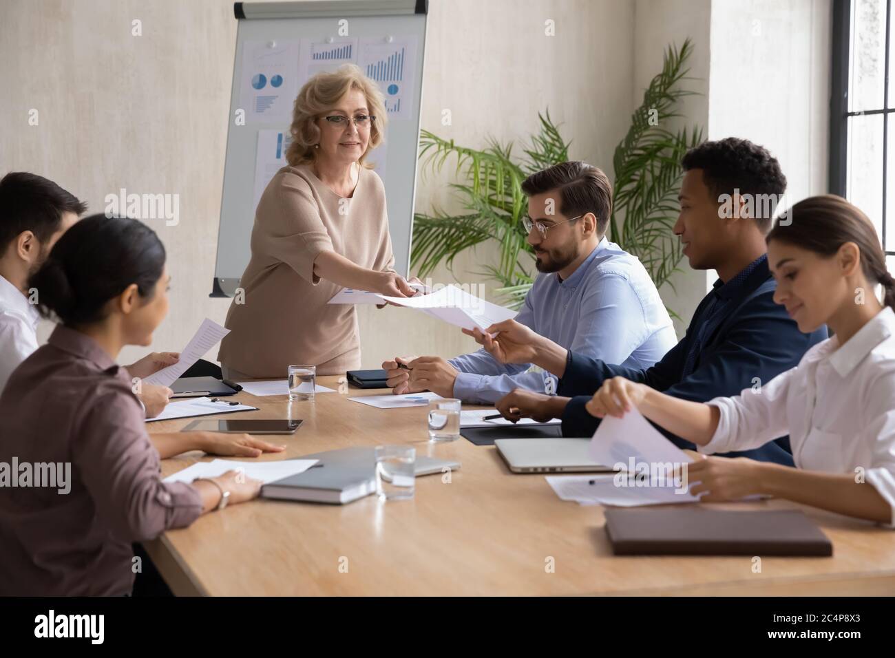 Middle aged businesswoman giving papers to employees at meeting Stock ...