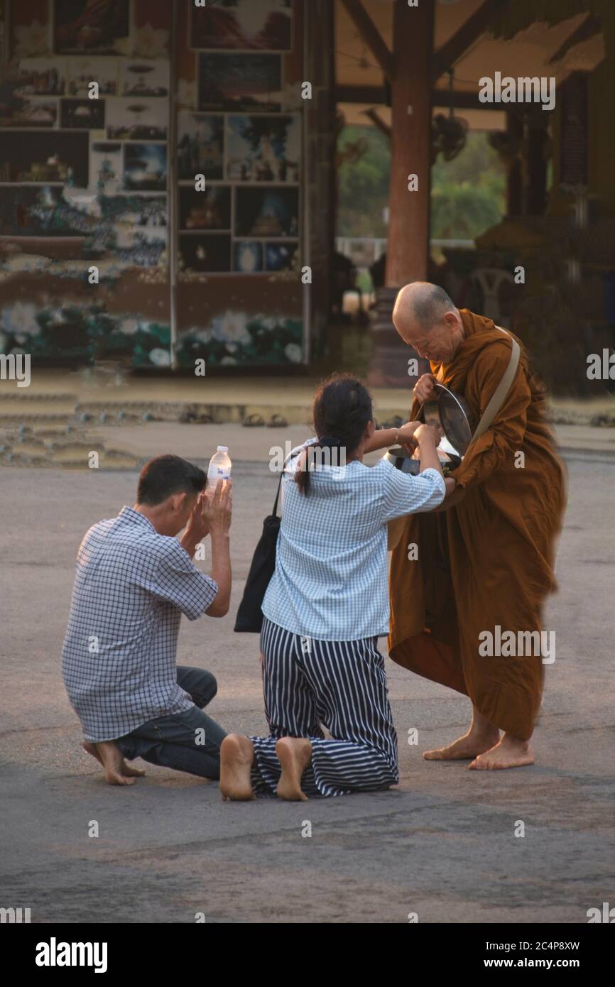 Couple kneeling in front of monk in street Offering food donation and ...