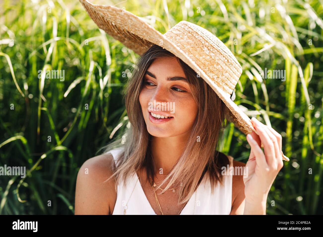 Young smiling woman wearing straw hat while sitting in park in front of ...
