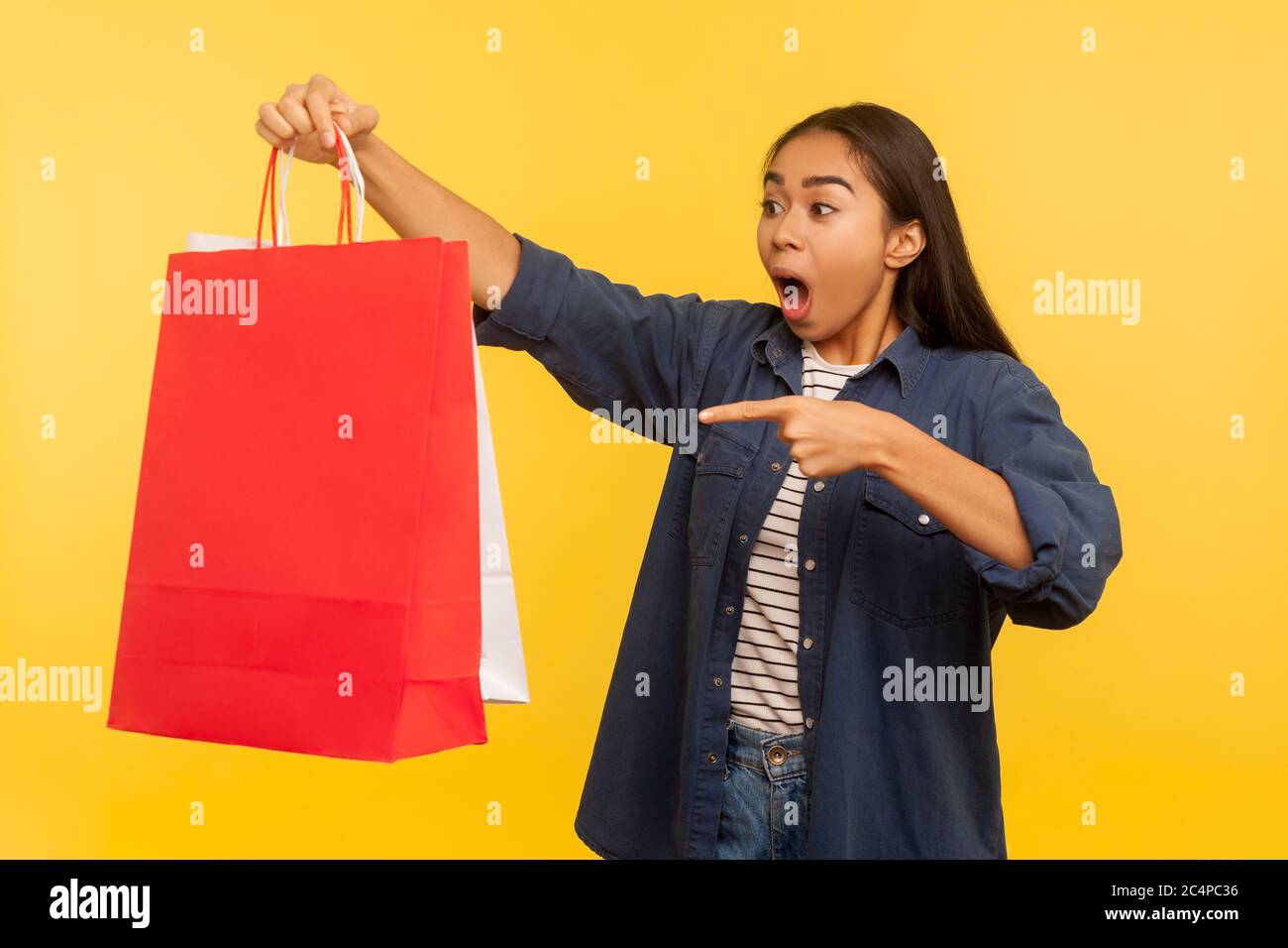 Portrait of amazed excited shopper girl in denim shirt pointing bags ...