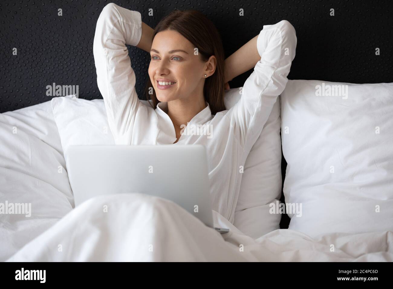 Happy female dreaming in bed working on computer Stock Photo - Alamy