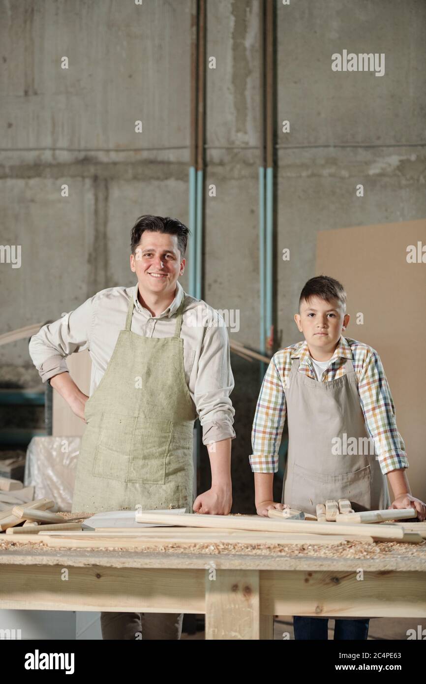 Portrait of smiling middle-aged carpenter and his teenage son in aprons ...