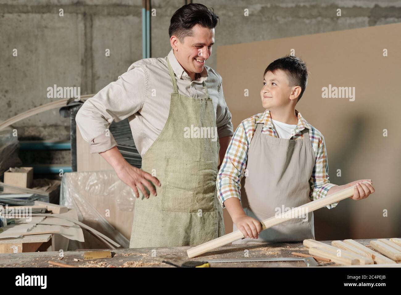 Smiling teenage boy in apron standing with polished wooden plank and ...