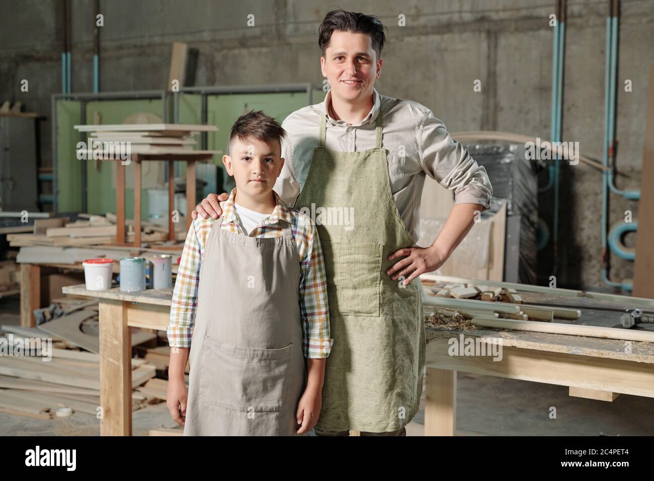 Portrait of positive middle-aged father in apron embracing his teenage ...