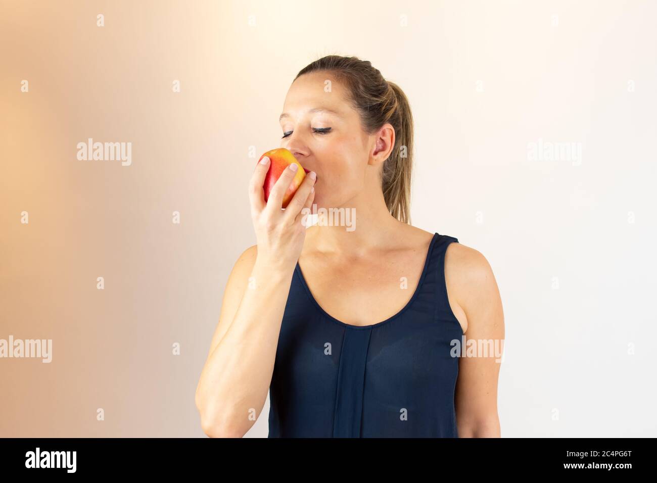 Woman in blue shirt taking bite of an apple Stock Photo - Alamy