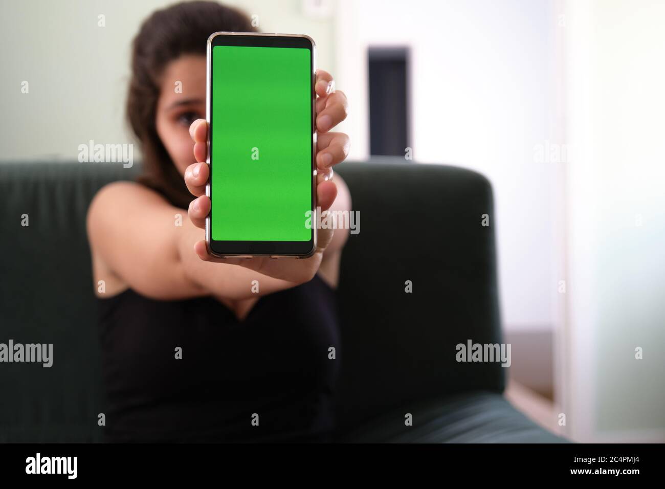Young caucasian woman hiding behind the smartphone with green screen ...