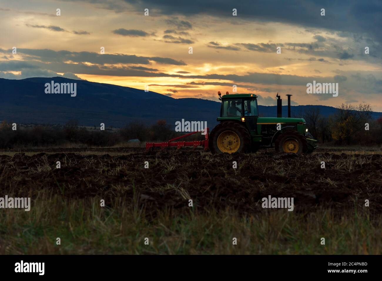 Tractor in sunset plowing the field Stock Photo - Alamy