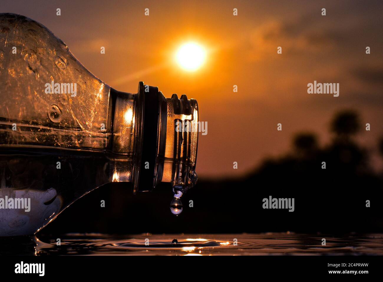 A droplet of water coming out from a bottle , reflection of the sun can ...