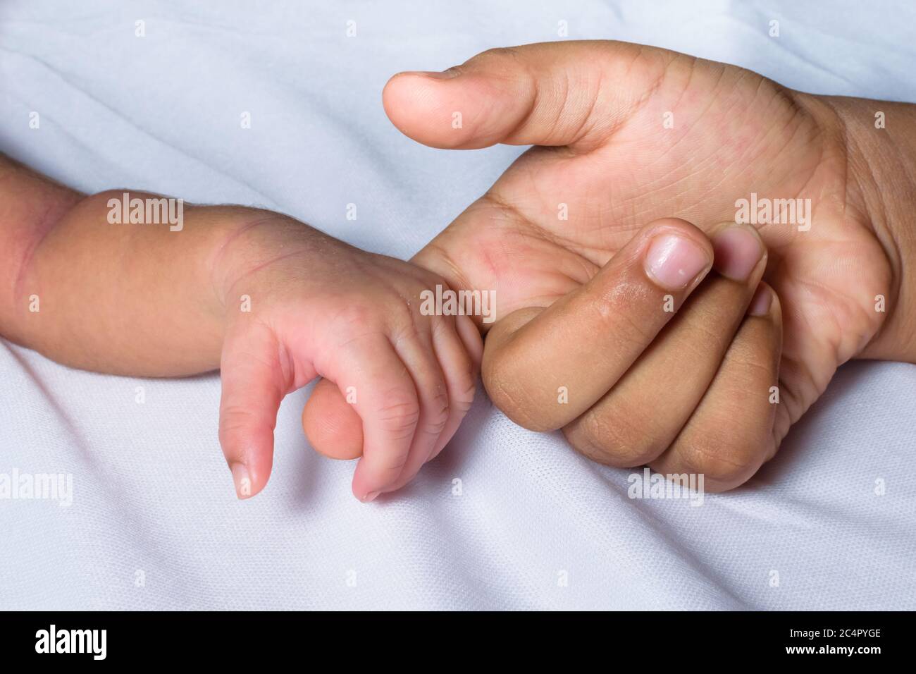 Index finger of a young boy held by a newborn baby in a white ...