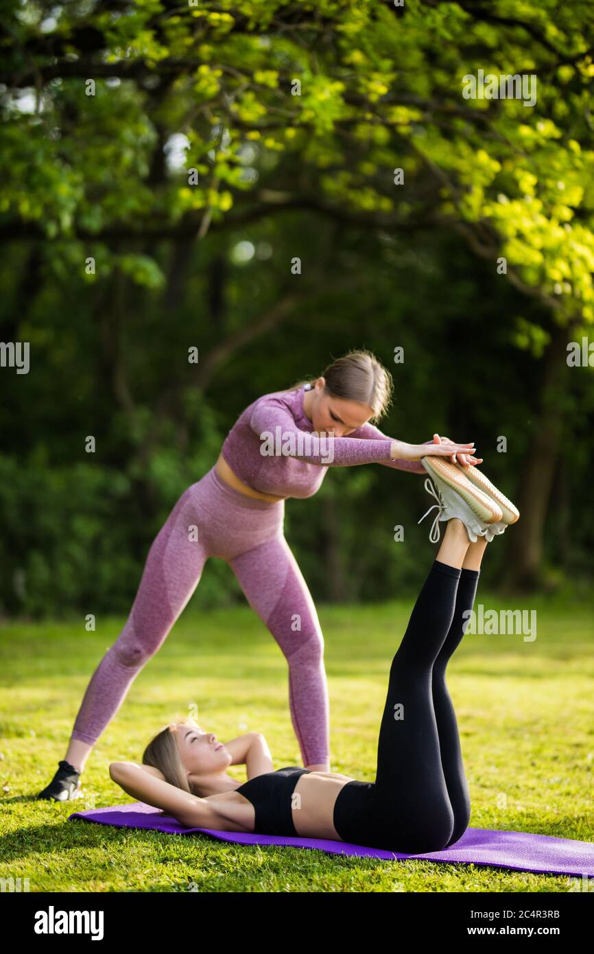 Young female friends helping each other to do some crunches before ...