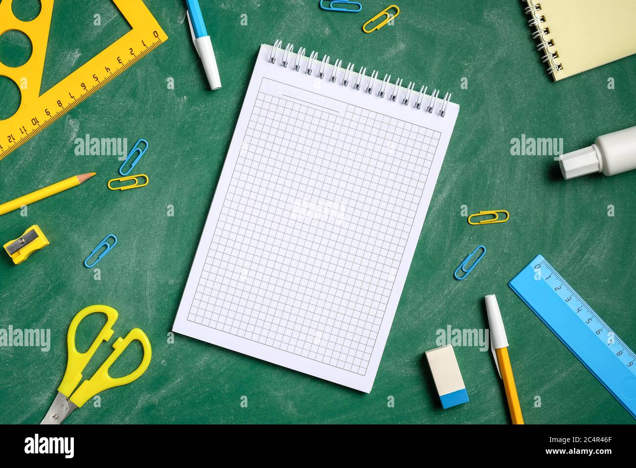Blank squared notebook and school stationery on green chalkboard ...