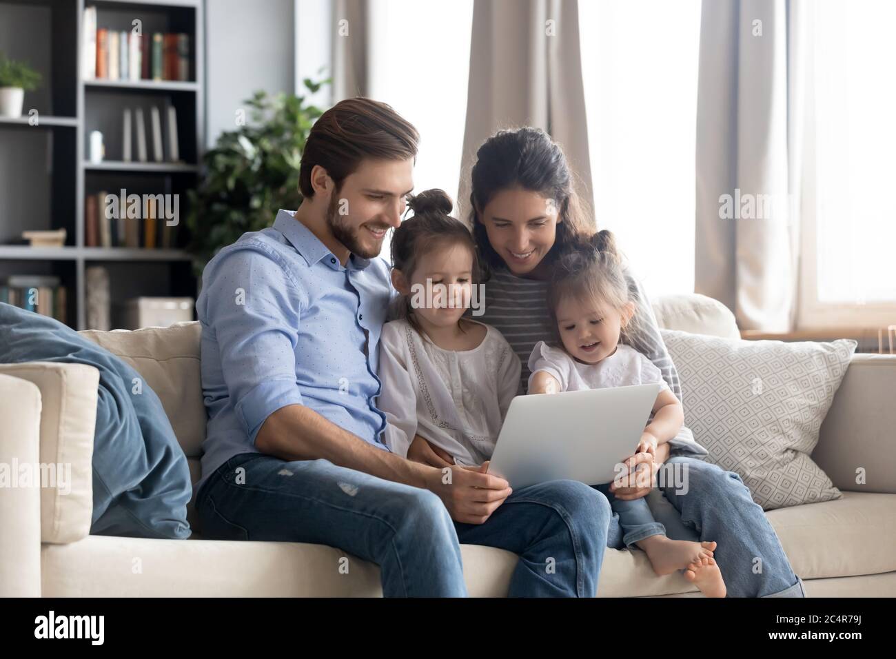 Happy young family with two little daughters using laptop together ...
