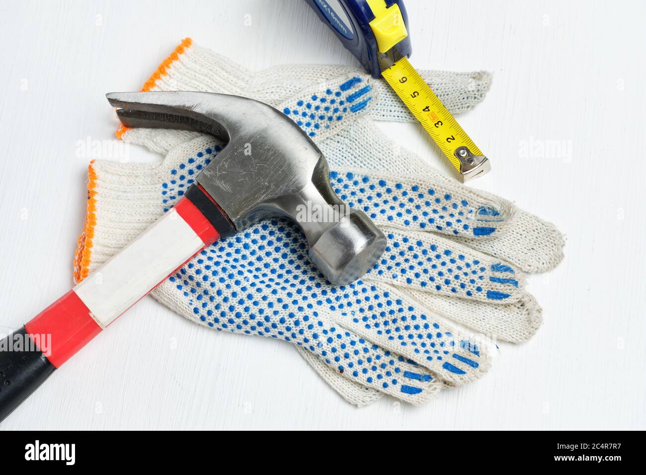 Hammer, measuring tape on work gloves and a white wooden background ...