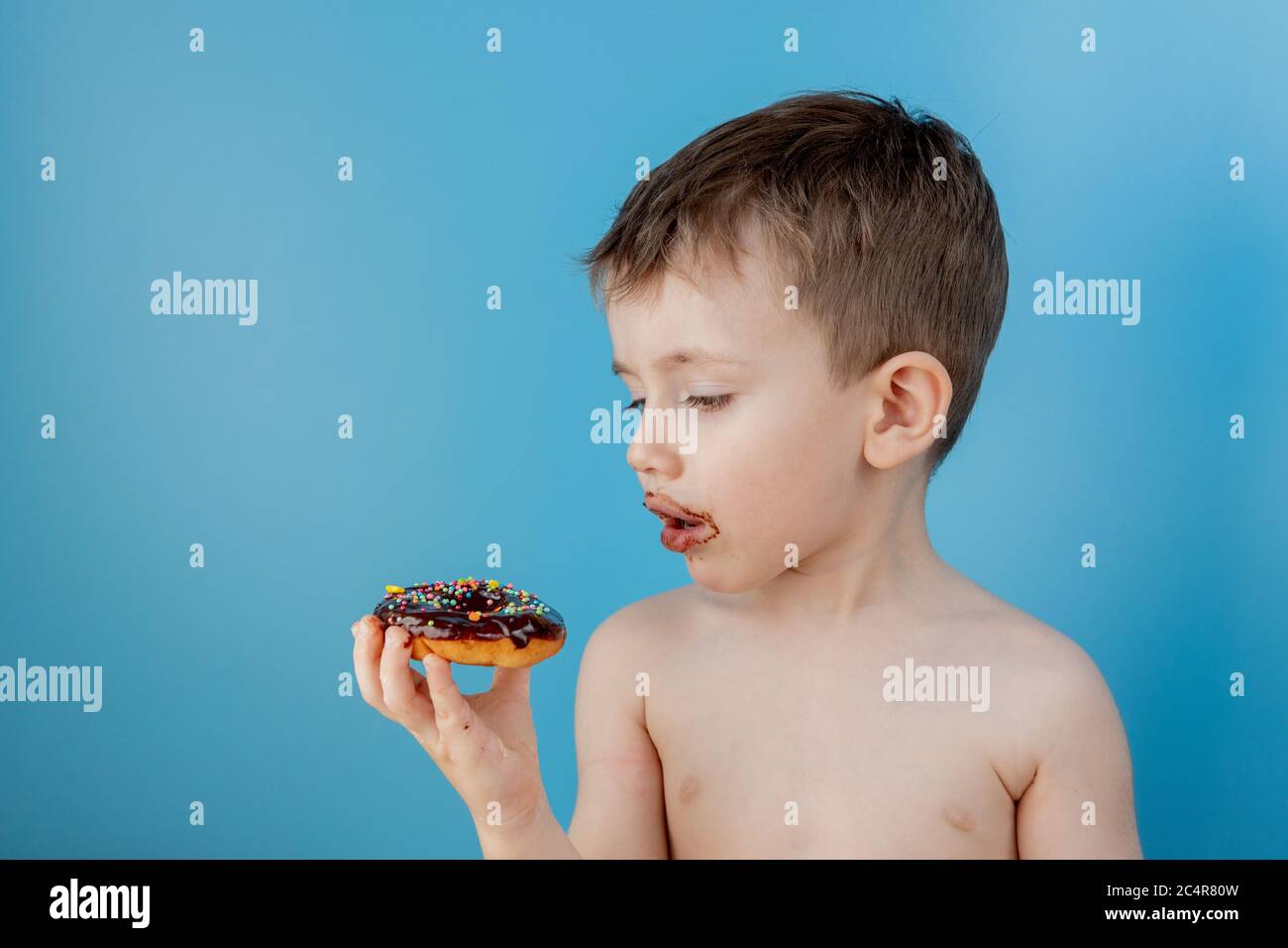Little boy eating donut chocolate on blue background. Cute happy boy ...