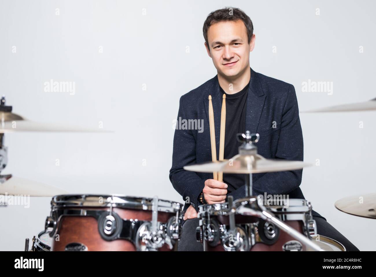 Young drummer behind drum set and plays the drums in studio smiling ...