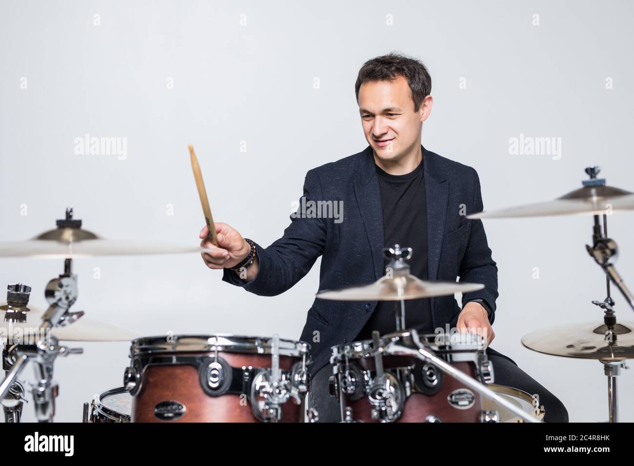 Young drummer behind drum set and plays the drums in studio smiling ...