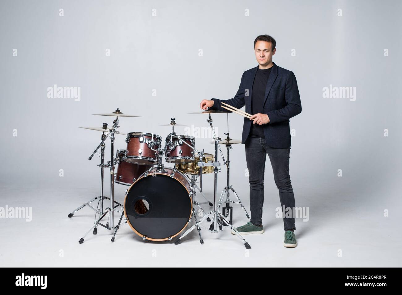 Smiling young man standing on drum set isolated on white background ...