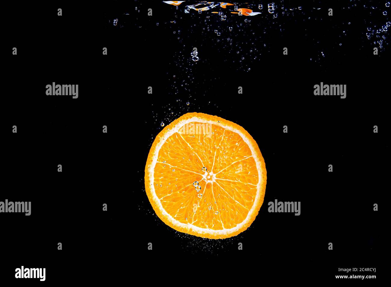 An orange falling into water on a black shiny background falls under ...