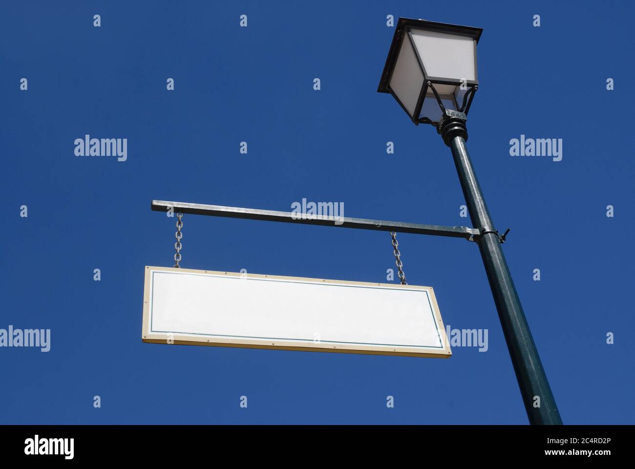 Old fashioned blank sign hanging from a lamp post against blue sky ...