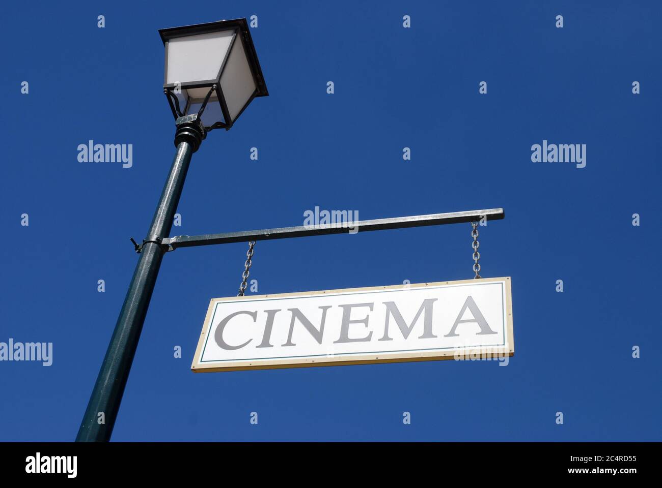 Old fashioned Cinema sign hanging from a lamp post against blue sky in ...