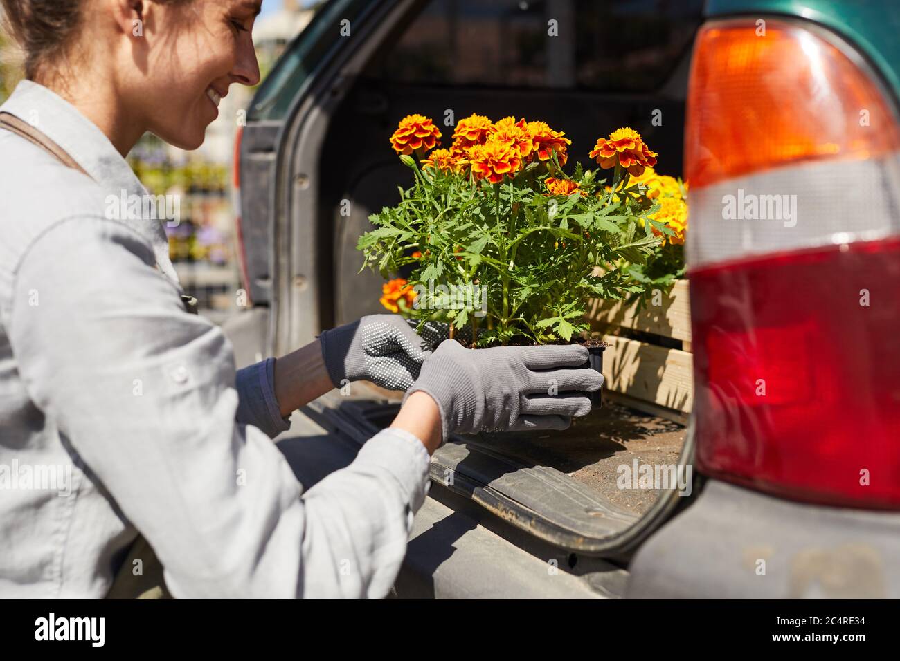 Side view portrait of smiling young woman loading flowers in car at ...