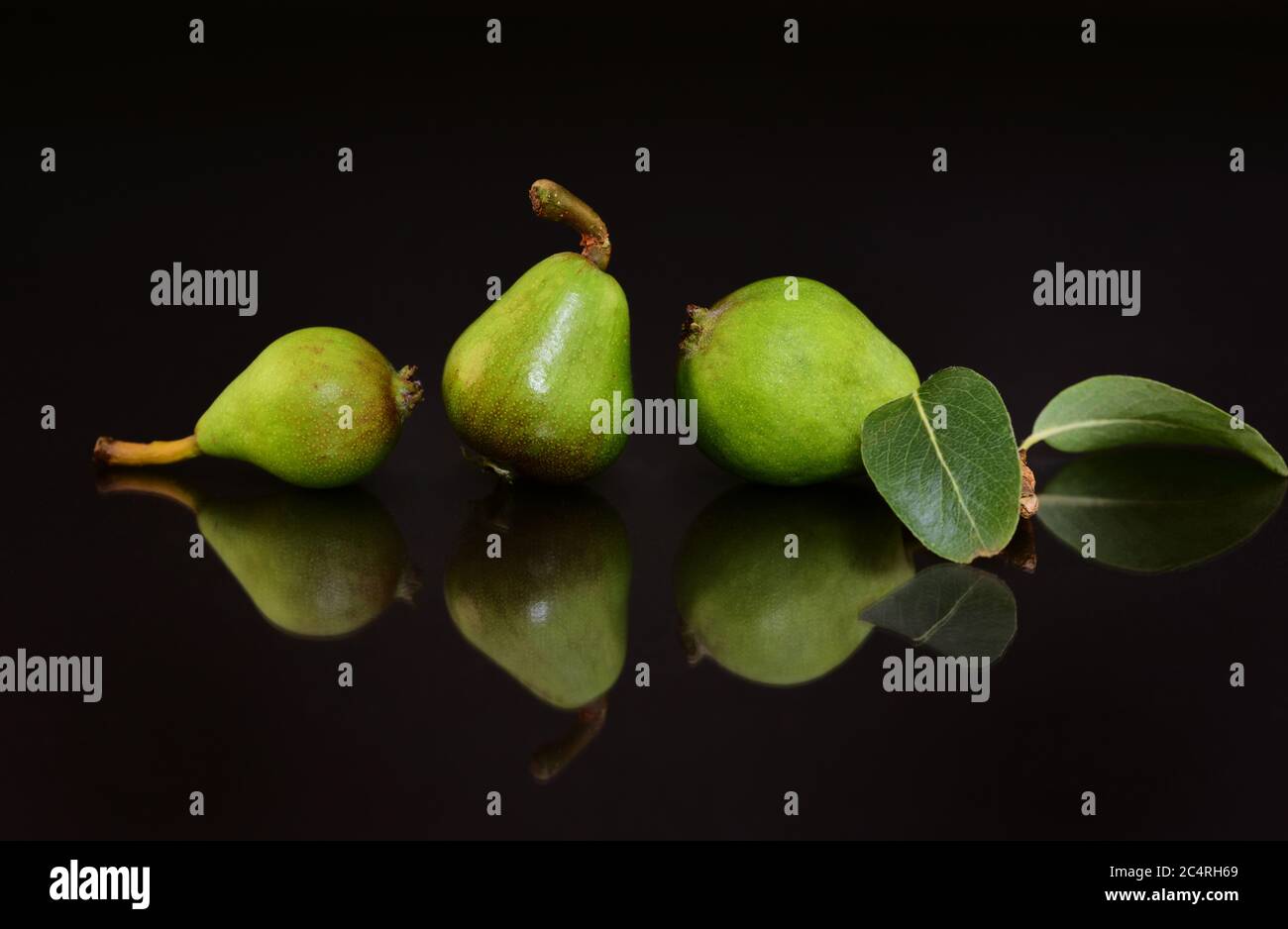 Three small green pears and a leaf lie against a dark background and ...