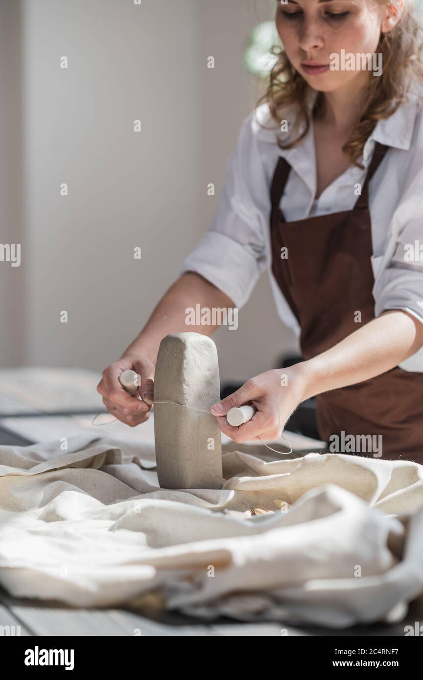 Female potter cutting piece of pottery clay using trimming tool close ...