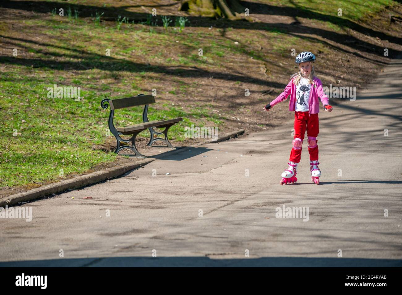 A young girl on roller blades and wearing protective equipment passes a ...