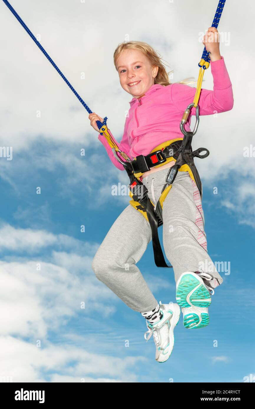 A Happy Young Blonde Girl Bouncing While Attached To Bungee Cords Blue