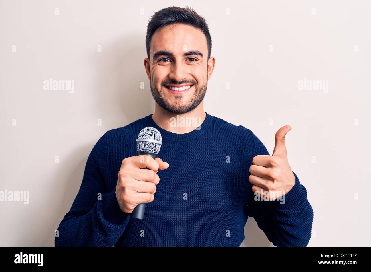 Young handsome singer man with beard singing song using microphone over white background smiling ...