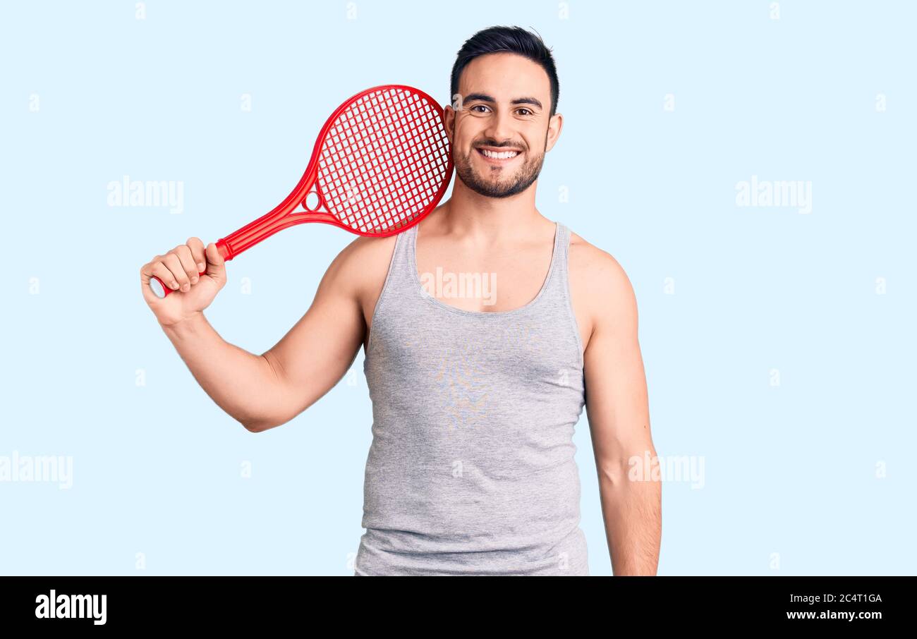 Young handsome man holding tennis racket looking positive and happy ...