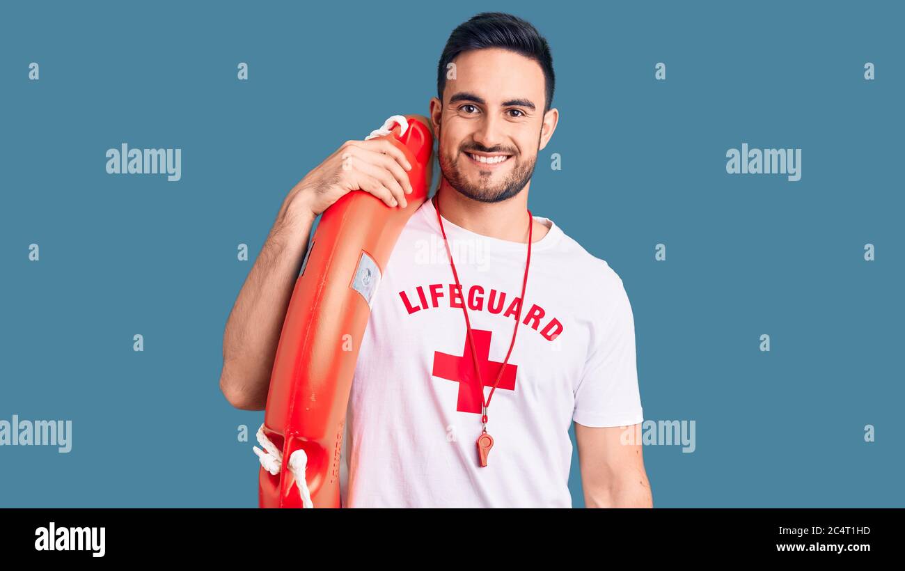 Young handsome man wearing lifeguard uniform holding float looking ...