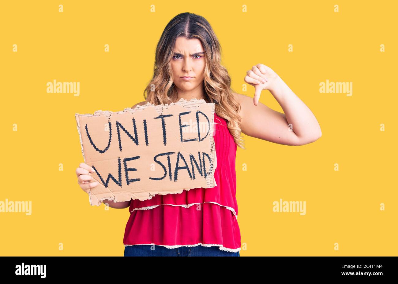 Young caucasian woman holding united we stand banner with angry face ...