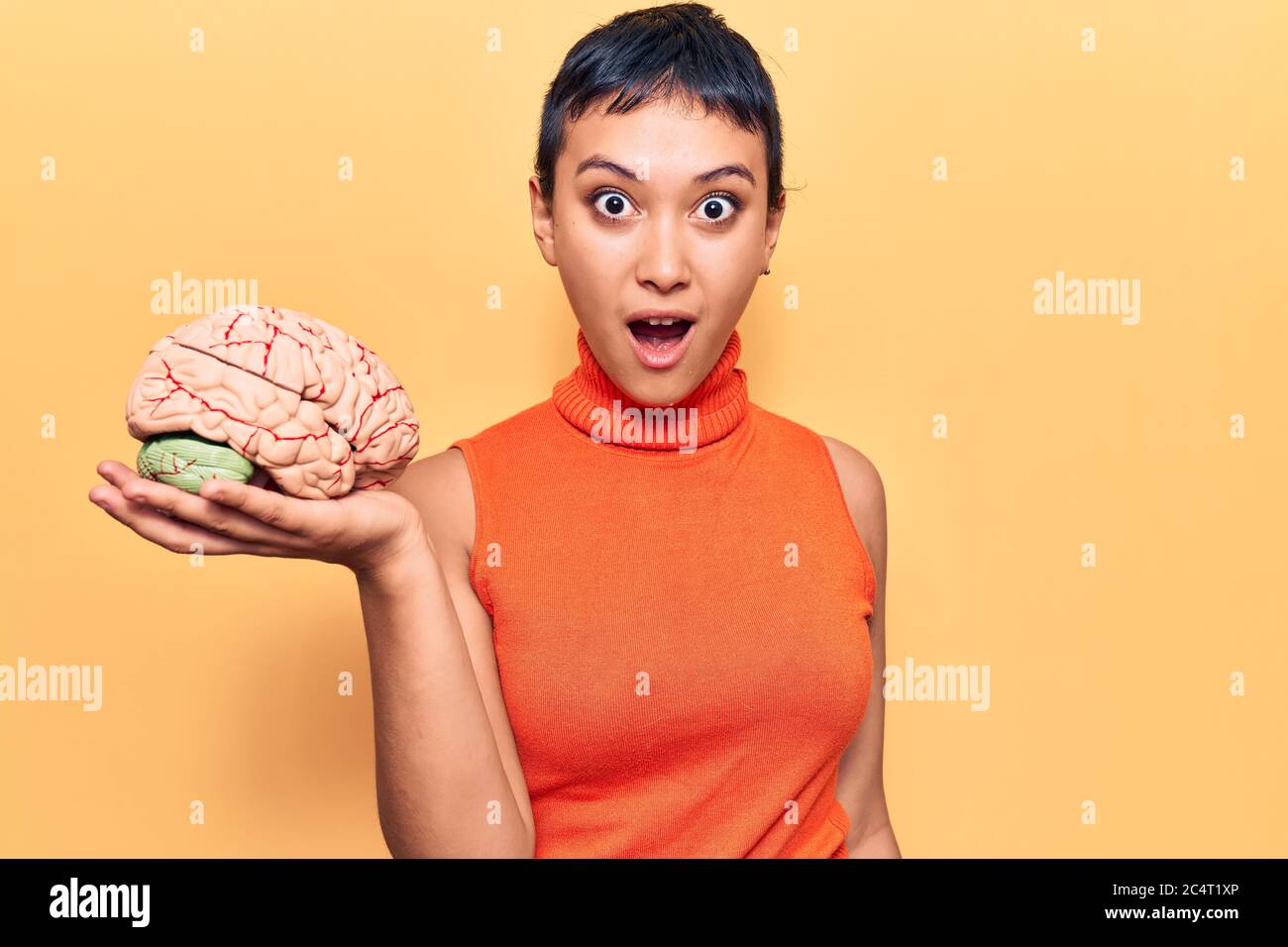 Young woman holding brain scared and amazed with open mouth for ...