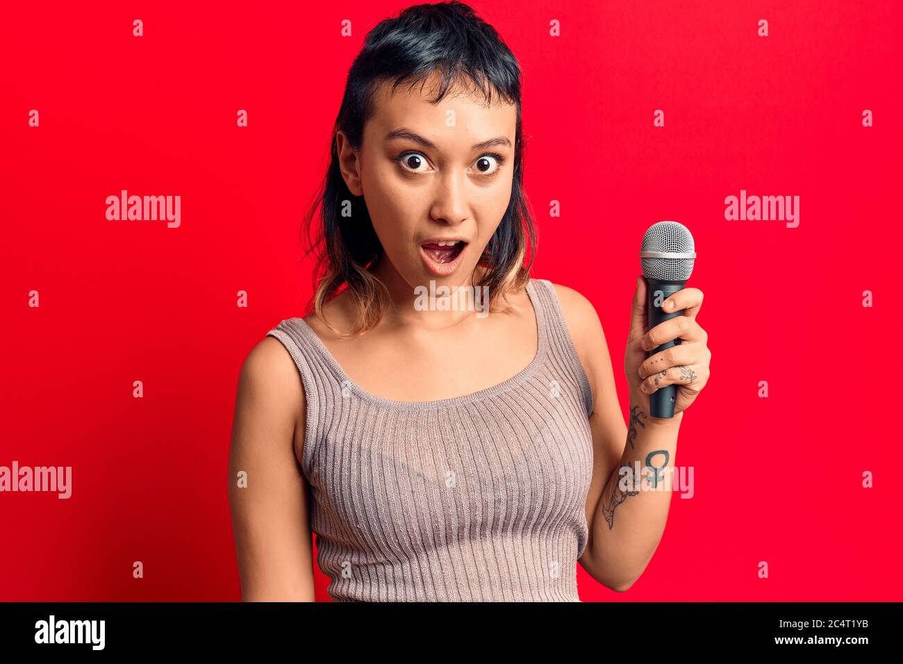 Young woman singing song using microphone scared and amazed with open ...