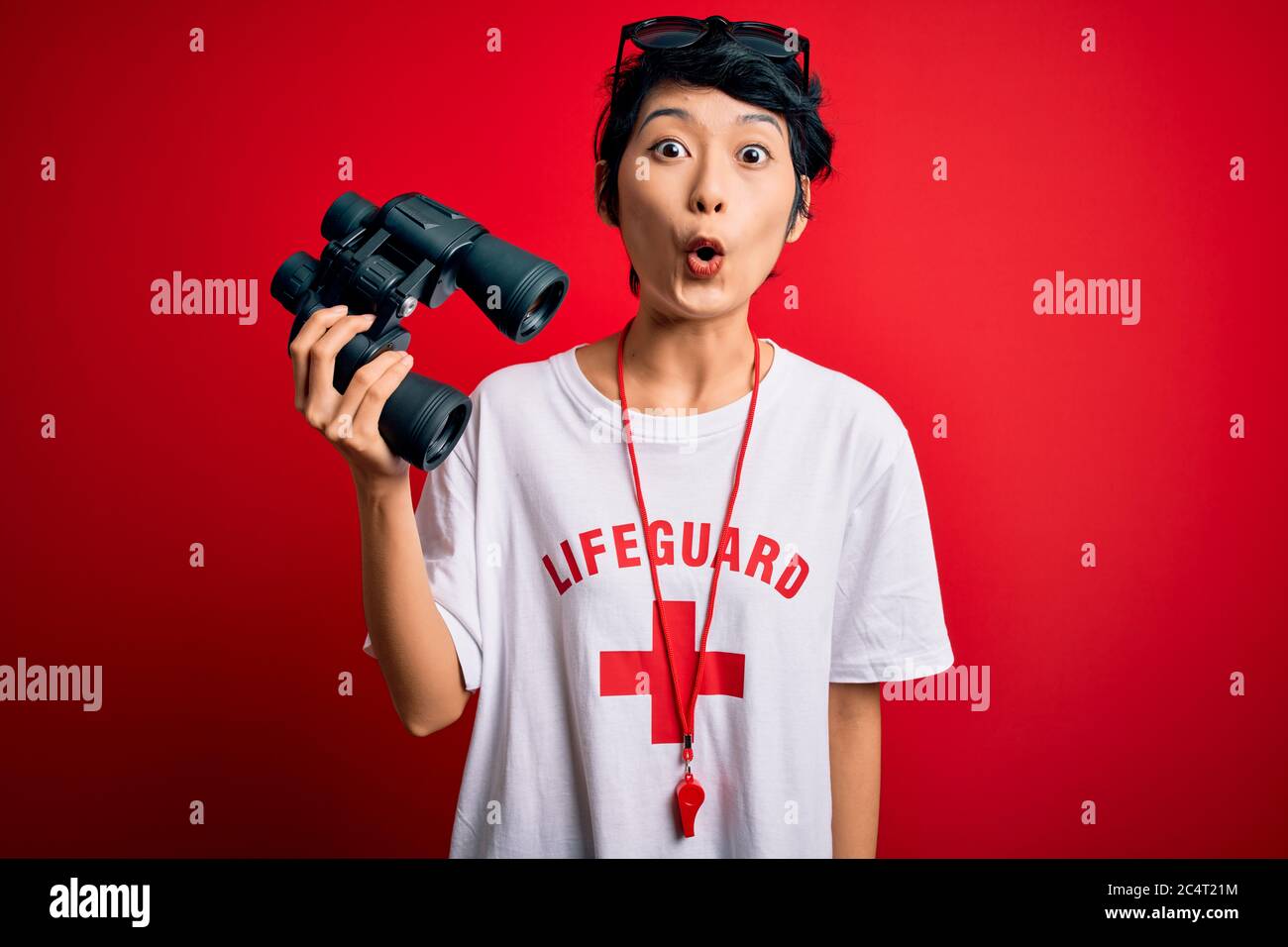 Young beautiful asian lifeguard girl using whistle and binoculars over ...