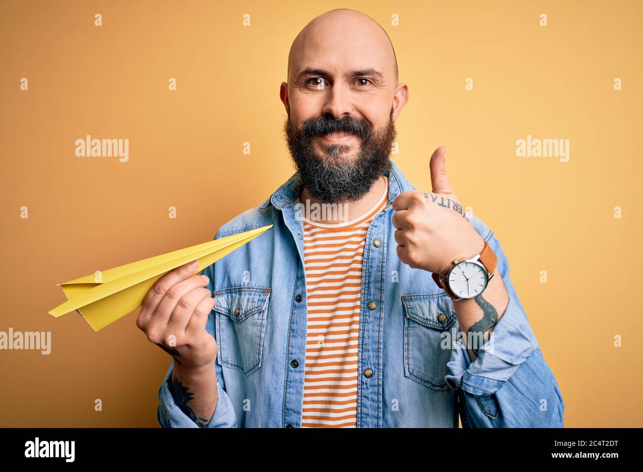 Handsome bald man with beard holding paper airplane over isolated ...