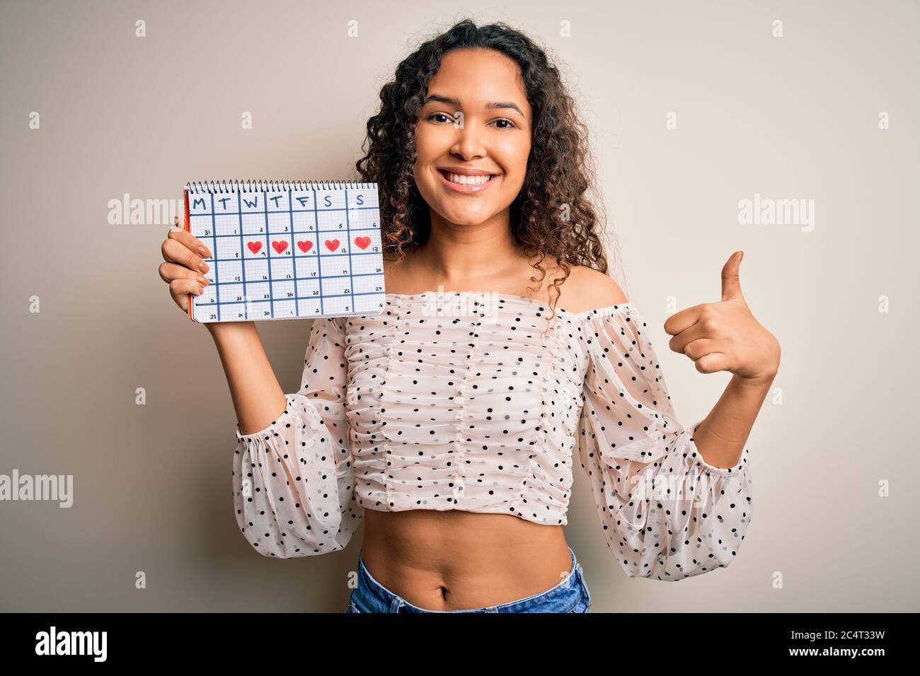 Young beautiful woman with curly hair holding mensturation calendar ...