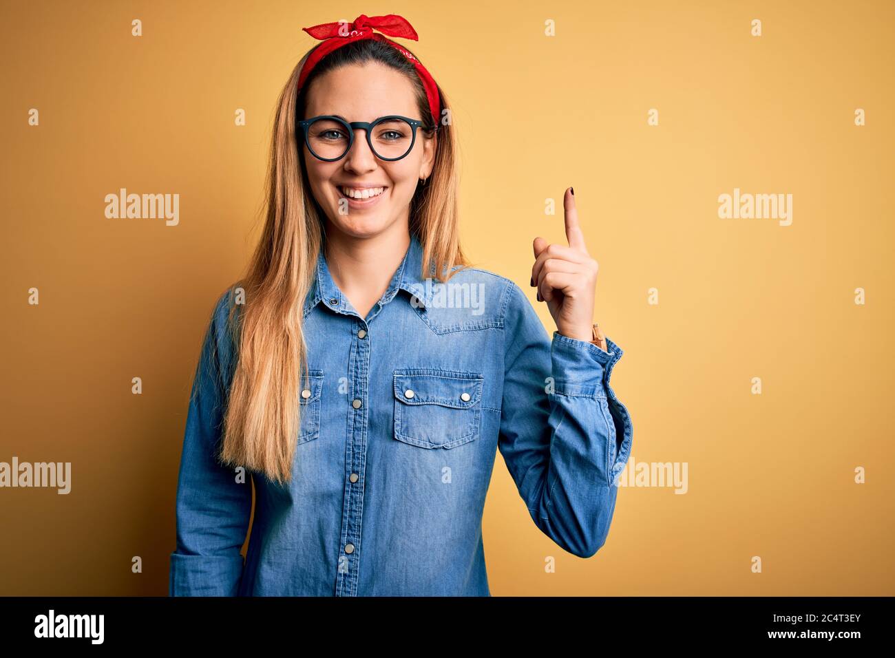 Young beautiful blonde woman with blue eyes wearing denim shirt over ...