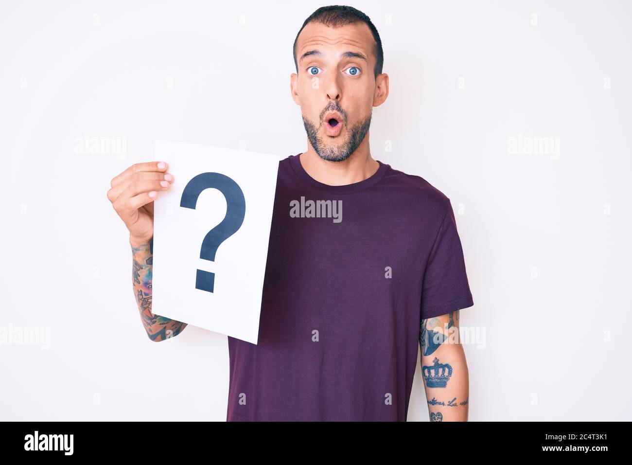 Young handsome man with tattoo holding question mark scared and amazed ...