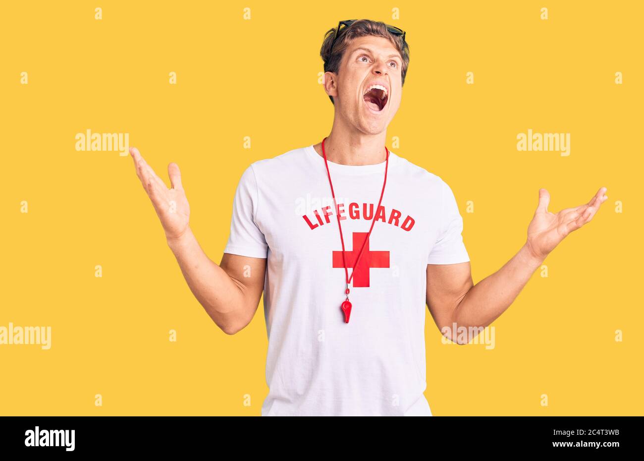 Young handsome man wearing lifeguard t shirt and whistle crazy and mad ...