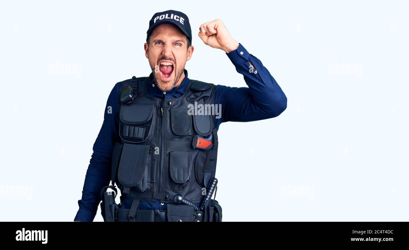 Young handsome man wearing police uniform angry and mad raising fist ...
