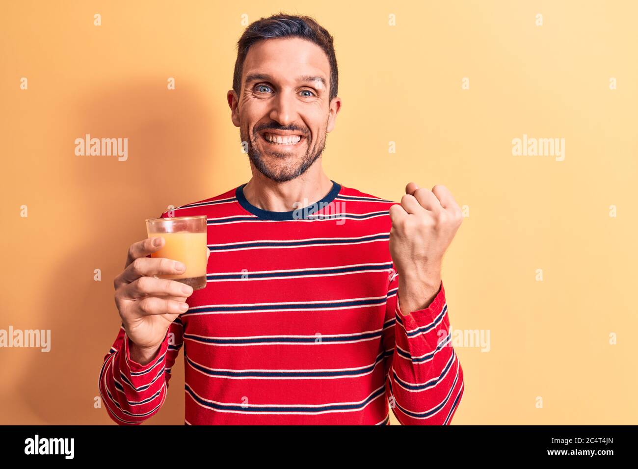 Young handsome man drinking glass of healthy orange juice over isolated ...