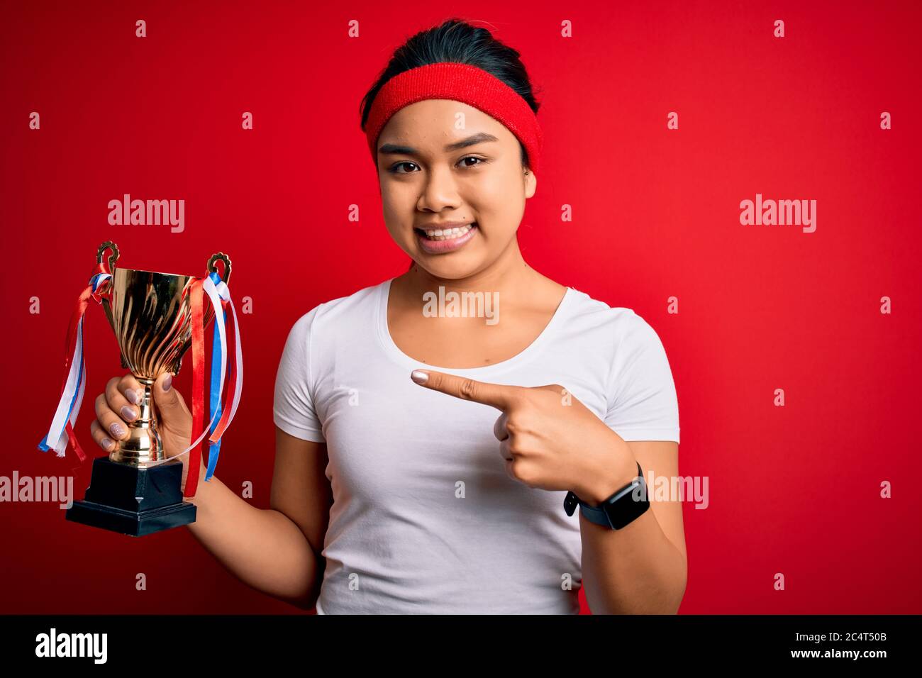 Young champion asian girl winning trophy cup standing over isolated red ...