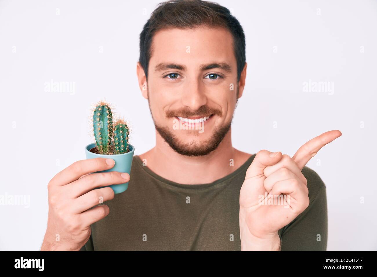 Young handsome man holding small cactus pot smiling happy pointing with ...